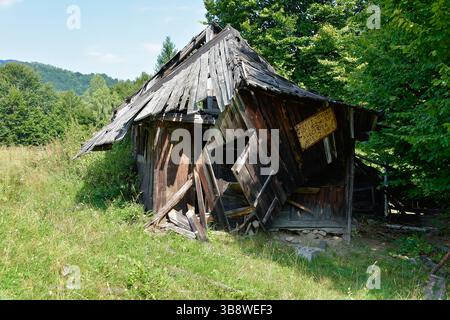 Old wooden cabin with severely collapsed roof and leaning walls on a ...