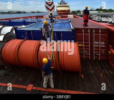 Crane unloads rolls of PVC cable sheathing from cargo ship. Workers ...