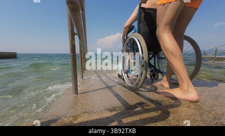Lifeguard helping a woman with disability enter the water across the ...