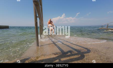 Relaxed woman with disability, exiting the sea water with the help of ...