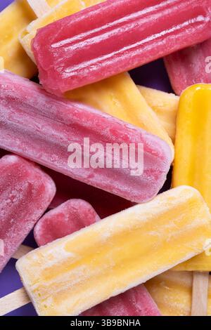Red strawberry popsicles and yellow popsicles on purple background ...