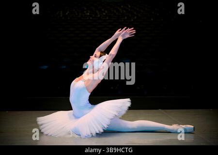 Ballet dancer in dramatic split pose with arms raised on theater stage ...