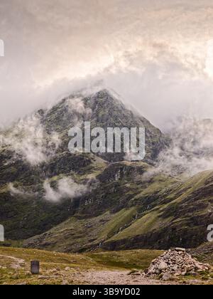 A scenic view of a rocky mountain enveloped in white clouds in a rural ...
