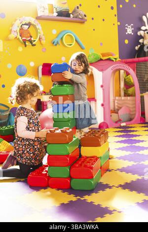Two girls play with big bricks in playroom Stock Photo - Alamy