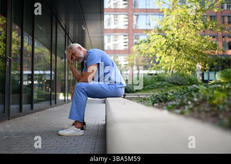 Frustrated and burnt-out doctor sitting outside the hospital, feeling ...