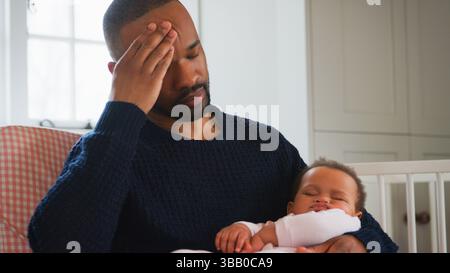 Stressed New Father Sitting In Chair Holding Sleeping Baby Girl In ...