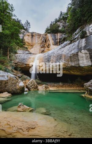 Secluded waterfall cascading into turquoise grotto pool. Limestone cave ...