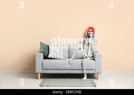 Human skeleton in colorful wig sitting on sofa and watching TV near ...