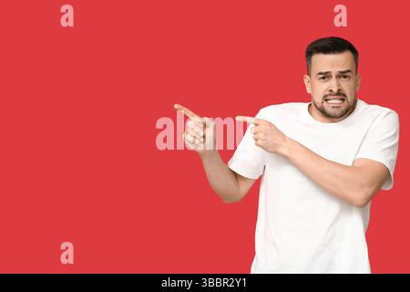 Handsome ashamed young man pointing at something on brown background ...