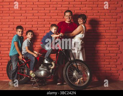 Big and happy family on motorcycle at red background of brick wall ...