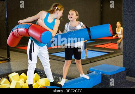 Tween girl fighting by pugil stick with female friend on inflatable ...