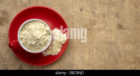 Whey protein powder in a red coffee cup against textured bark paper ...