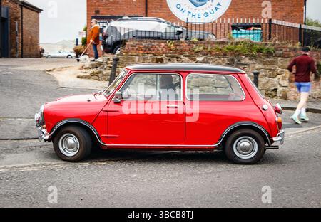A vibrant red classic Mini Cooper with white roof, buildings black ...