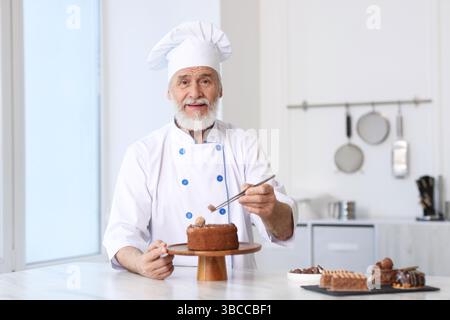 Elderly pastry chef decorating tasty desserts with edible gold leaf ...