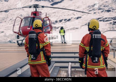 Firefighters in full gear stand by on a street with parked cars and a ...