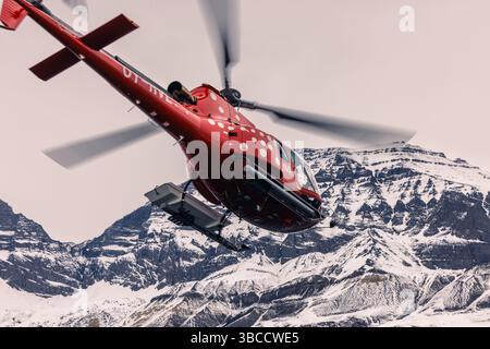 Red helicopter flying low above icy terrain and jagged peaks in West ...