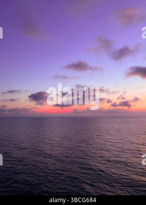 Purple sunset sky over the calm sea with autumn trees on the shore ...
