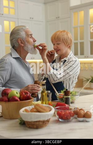 Senior couple feeding each other while cooking in kitchen Stock Photo ...