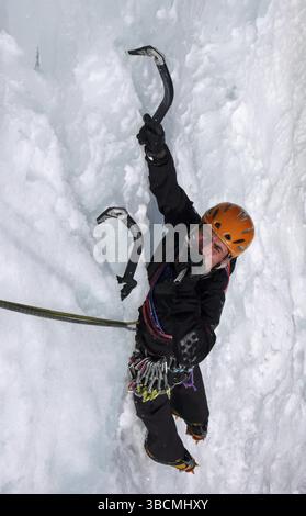 male ice climber on a steep frozen waterfall on a beautiful winter day ...