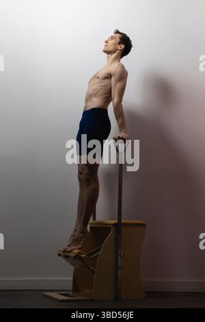 Slim male ballet dancer trains on Pilates equipment. Elegant pose, core ...