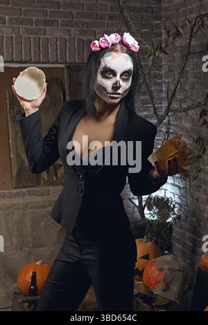Woman in gothic costume and sugar skull makeup looking at camera on red ...