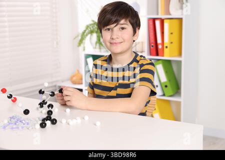 Boy making DNA structure model at desk indoors, closeup. Space for text ...