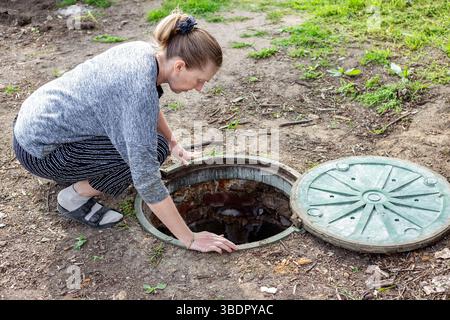 A woman looks into an open septic tank to check the level of sewer ...