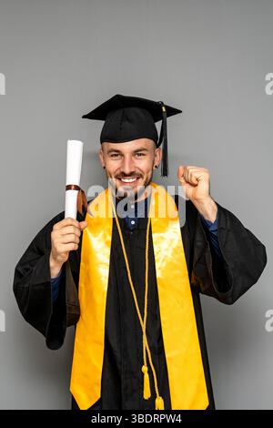 Happy graduated man in a black gown jumping while holding his diploma ...