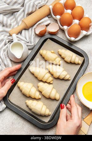 top view of tray with croissants, rolling pin and baking paper on black ...