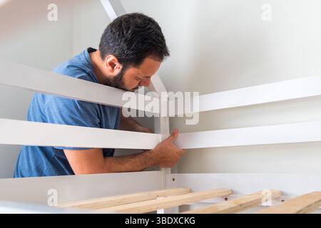 A man is fixing a bed frame. The bed is white and the frame is made of ...