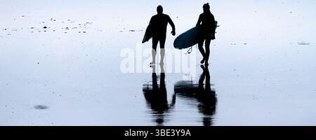 A panoramic image of two surfers walking in the sea at Fistral Beach on ...