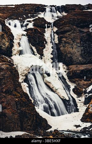 A vertical shot of a waterfall flowing down the wall in a forest ...