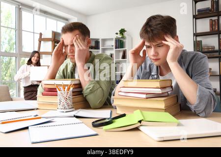 Stressed male students with books at table in library Stock Photo - Alamy
