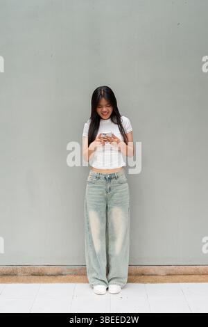 Portrait of a teenage Asian woman using a tablet, wearing headphones to ...