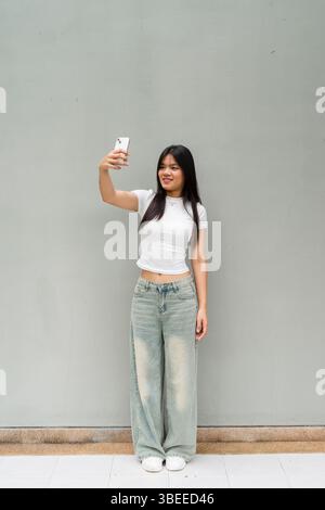 Portrait of a teenage Asian woman using a tablet, wearing headphones to ...