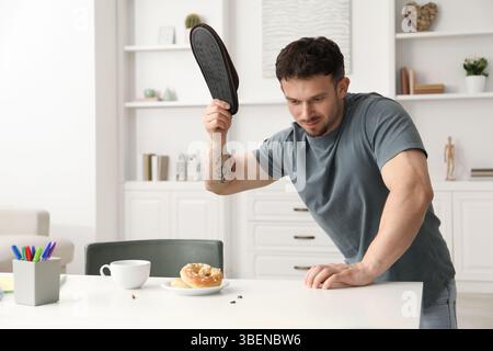 Emotional young man killing cockroaches with slipper at white table ...