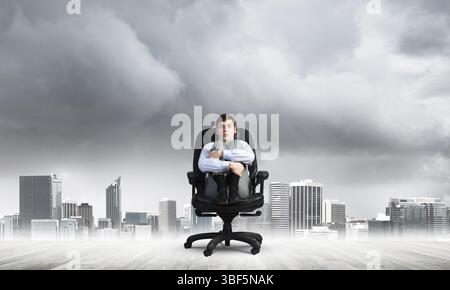 Scared businessman sitting on a chair with his hands clasped his knees ...