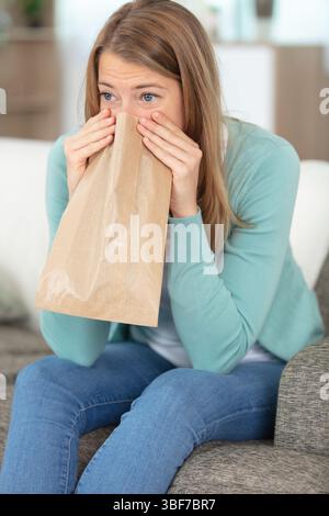 young woman breathing into paper bag while suffering from panic attack ...