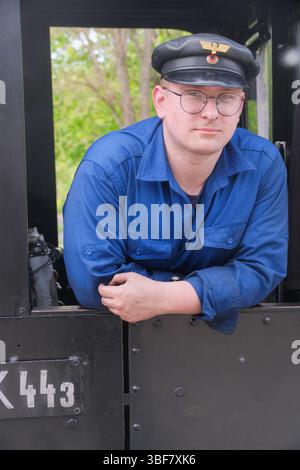 A train engineer in blue overalls crouching down and applying motor oil ...