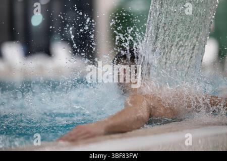 Man standing under a hydrotherapy waterfall in a spa pool, receiving ...