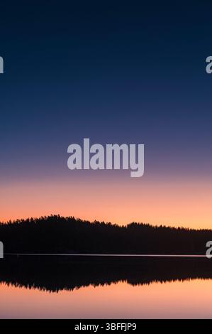 At dawn, a quiet lake surrounded by dense forest near Gothenburg ...