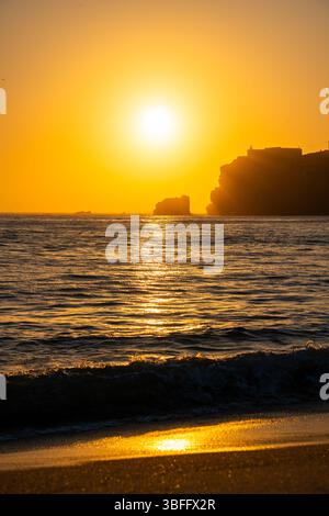 The sun sets over the beach, casting light through dark clouds ...