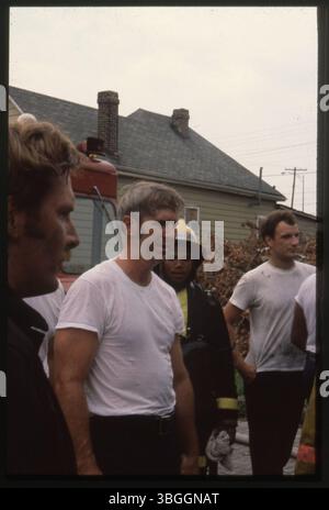 Firefighters in protective gear stand in front of a damaged building ...