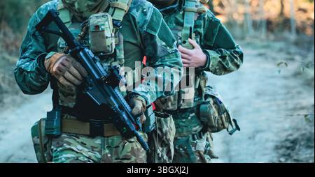 Two soldiers patrolling through the dense forest, one gripping a rifle ...