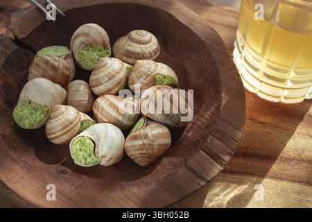 Snails cooked with herb oil on a wooden plate, served with white wine ...