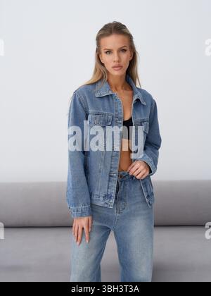 A stylish blonde woman models her denim outfit while sitting on a stool ...