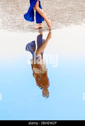 Person walks in shallow water at sunset, with waves and a tranquil ...