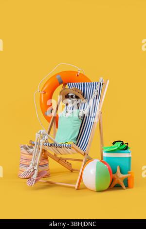 Human skeleton with beach accessories and deck chair on yellow ...