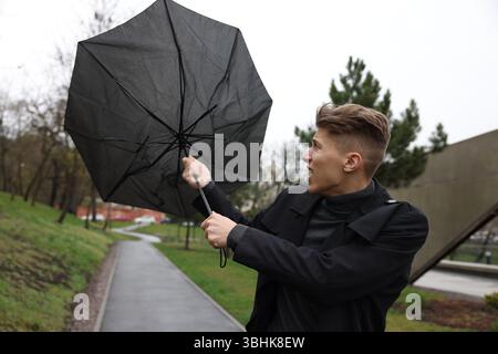 Man with broken umbrella fighting wind under rain outdoors Stock Photo ...