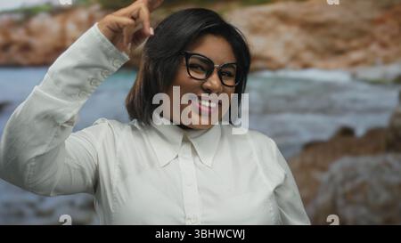 Woman smiling at seaside makes salute gesture wearing glasses with ...